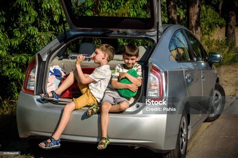 행복한 두 아이 소년과 그의 동생은 자동차 트렁크에 함께 앉아 가족 차량 수하물 칸에서 서로 껴안고 있는 쾌활한 아이들 주말 여행 및 휴일 개념 소년에 대한 스톡 사진 및