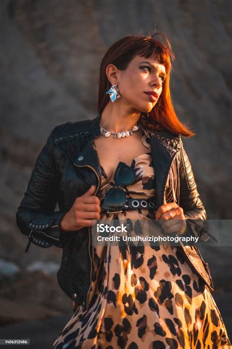 바다 옆에 표범 드레스를 입고 젊은 갈색 머리 백인 여성의 바위 옆에 해변에서 여름 거리 스타일 바스크 국가 데바 마을의 사코네타 해변 오른쪽을 바라보며 가방에 대한 스톡