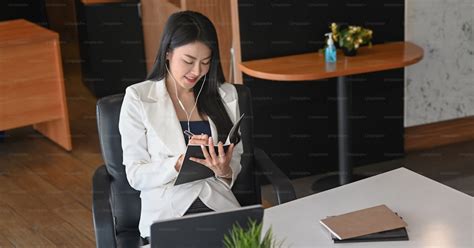 이어폰을 끼고 직장에 앉아 노트북으로 근무일을 계획하는 행복한 사업가 사진 Unsplash의 테이블 이미지