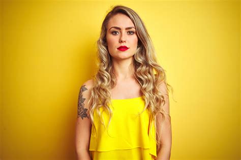 노란 고립 된 배경 위에 서있는 티셔츠를 입은 젊은 여성은 얼굴에 심각한 표정으로 편안합니다 카메라를 보는 간단하고 자연스러운 T 셔츠에 대한 스톡 사진 및 기타 이미지