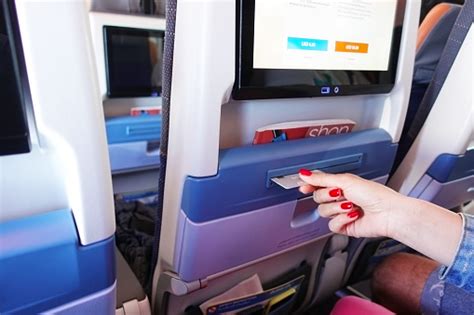 비행 중 비행기 안에서 앞 좌석 뒤에 있는 현대 터미널을 통해 신용 카드로 지불 하는 여자 Brand Name Mobile
