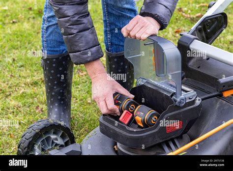 Woman Puts Freshly Charged Battery In A Lawn Mower Battery Compartment