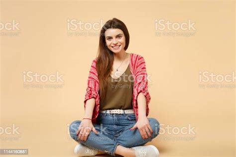 앉아 캐주얼 옷에 아름 다운 젊은 여자 미소의 초상화 스튜디오에서 파스텔 베이 지 벽 배경에 고립 된 찾고 카메라 사람들은
