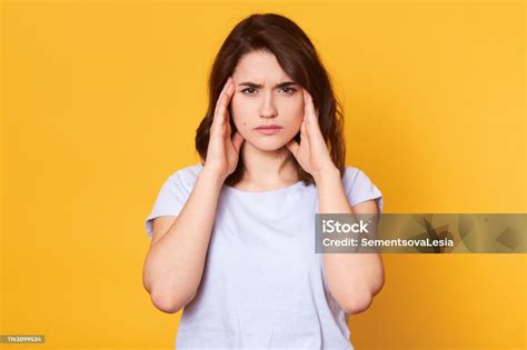 두통을 가진 여자는 문제가 고통을 가진 여자 서 사원에 양손을 유지 합니다 갈색 머리 여자 절반 길이 초상화입니다 노란색 배경 위에 고립 인간의 감정 얼굴 표정 개념 감정에