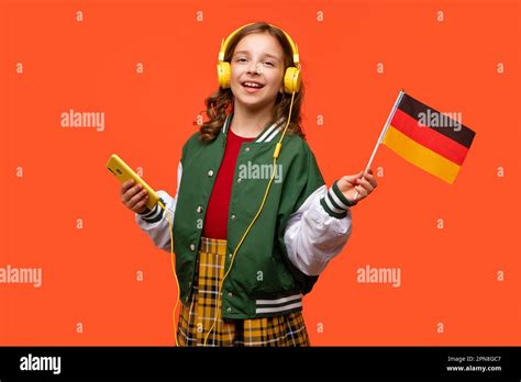 Teen School Girl In Casual Clothes And Headphones Holds Small National Flag Of Germany And