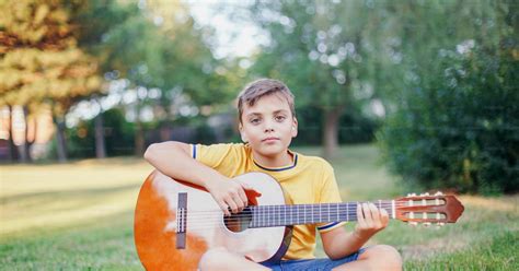 야외에서 기타를 연주하는 십대 초반의 소년을 듣기 어렵습니다 귀에 보청기를 착용한 아이는 공원에서 음악을 연주하고 노래를 부릅니다 어린이 어린이를위한 취미 예술 활동