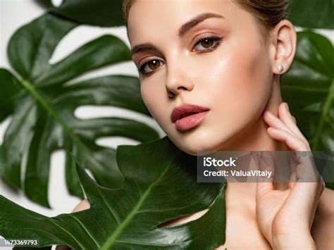 깨끗하고 건강한 피부를 가진 아름다운 어린 소녀의 초상화 백인 소녀의 깨끗한 얼굴 클로즈업 아름 다운 여자는 그녀의 손으로 그녀의 얼굴을 만진다 몸 근처에 녹색 잎이있는