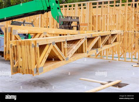 telehandler crane raises wooden trusses at construction site during