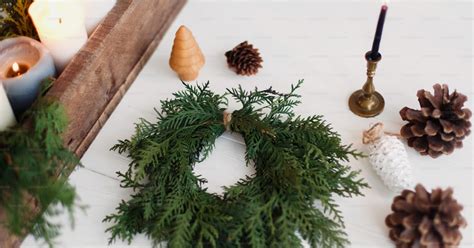 흰색 나무 테이블에 양초 솔방울 실 및 장식품이 있는 소박한 크리스마스 화환 삼나무 가지로 심플하고 세련된 크리스마스 화환 만들기 휴일 워크샵 강림절 사진