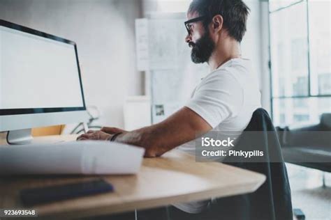 젊은 수염 눈 안경을 현대 로프트 스튜디오데스크톱 컴퓨터와 사무실에서 일 하는 전문 건축가 화이트 빈 화면을 표시 합니다 흐리게 배경입니다 수평 건축가에 대한 스톡 사진 및