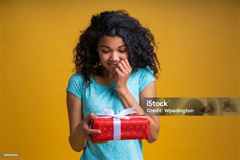 호기심 많은 얼굴 표정으로 새틴 리본으로 장식된 선물 상자를 들고 있는 아름다운 캐주얼한 옷을 입은 어두운 피부 소녀의 초상화