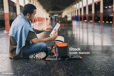 기차역 바닥에 앉아 디지털 태블릿을 가진 젊은 남자 여행자가 어디로 갈지 선택합니다 배낭 여행자의 개념은 기차로 모험을 여행합니다 40 44세에 대한 스톡 사진 및 기타
