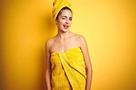 몸에 샤워 타월을 입고 아름다운 여자는 섹시한 표정 쾌활하고 행복한 얼굴로 카메라를보고 윙크 노란색 고립 된 배경 윙크를 통해 머리 수건에 대한 스톡 사진 및 기타 이미지
