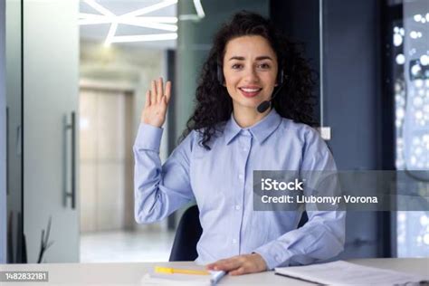 한 젊은 무슬림 여성이 헤드셋을 착용한 카메라 앞 책상에 앉아 있다 인사하고 카메라를 향해 손을 흔들고 소통합니다 온라인 인터뷰 일 공부 팟 캐스트 녹음 블로그 35 39