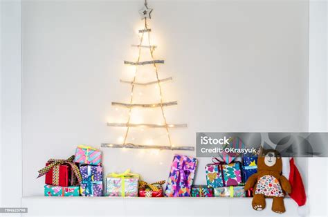 축제 조명 화려한 선물 상자 산타 모자곰 장난감 흰색 벽에 매달려 나무 막대기로 만든 현대 창조적 인 크리스마스 에코 트리 심플하고 미니멀한 인테리어 디자인과 어린이 방장식