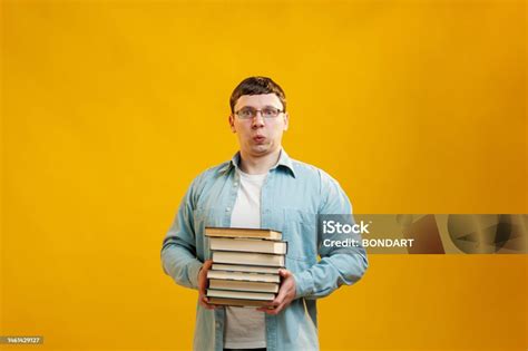 안경을 쓴 청년 학생이 노란색 배경에 대학 도서관의 대학 책 더미를 들고 있다 행복한 사람은 미소를 짓고 그는 졸업하게되어 기쁘고 해외 교육 개념입니다 복사 공간 30 34