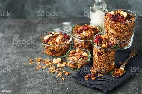 그릭 요거트 또는 우유와 캐슈 아몬드 호박과 함께 유리 병에 담긴 수제 그래놀라는 짙은 회색 테이블 배경에 말린 크랜베리 씨앗을 곁들인다 건강한 에너지 아침 식사 또는 간식