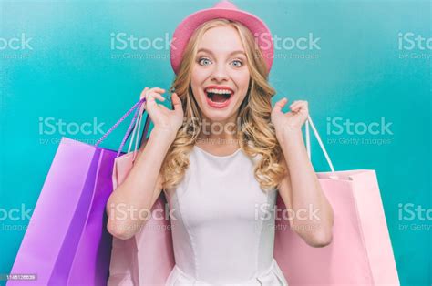 쾌활 하 고 매력적인 소녀는 그녀의 뒤에 화려한 가방을 들고 있다 또한 그녀는 분홍색 모자를 입는다 파란색 배경에 고립입니다 가방에 대한 스톡 사진 및 기타 이미지 Istock