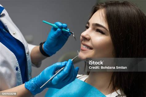 파란 장갑을 착용한 의사 치과 의사가 치과 용 거울과 비늘을 사용하여 여성 환자를 검사하고 클리닉에서 치과 의자에 앉아있는 동안