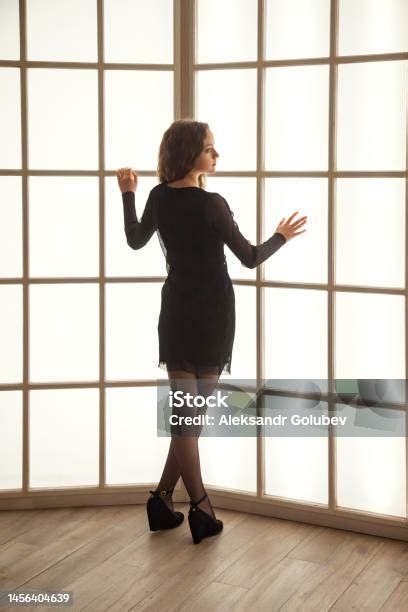뒷모습 전체 길이 외로운 십대 소녀가 검은 드레스를 입고 거실의 큰 창문 배경에서 포즈를 취하고 있다 스튜디오 촬영 혼자 세련