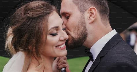 화려한 신부와 세련된 신랑은 비오는 야외에서 우산 아래에서 열정적으로 키스합니다 관능적 인 결혼식 커플을 포용합니다 신혼