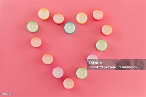 분홍색 배경에 하트 모양으로 배치 된 사용하지 않는 여러 가지 빛 왁스 티 라이트 촛불의 행의 상단 보기 배경으로 새로운 물