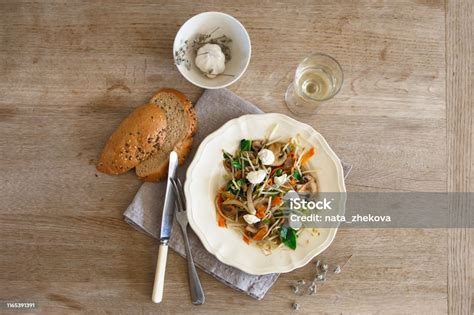 버섯과 코티지 크림 치즈를 곁들인 야채 볶음 요리 부드러운 버섯 볶음 요리는 나무 테이블에 화이트 와인과 빵과 흰색 접시에 제공