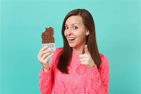 예쁜 젊은 여자에 파란색 벽 배경 스튜디오 초상화에 고립 된 손에 초콜릿 바 잡고 카메라에 분홍색 스웨터 포인팅 검지 니트 사람들의 라이프 스타일 개념입니다 복사 공간을