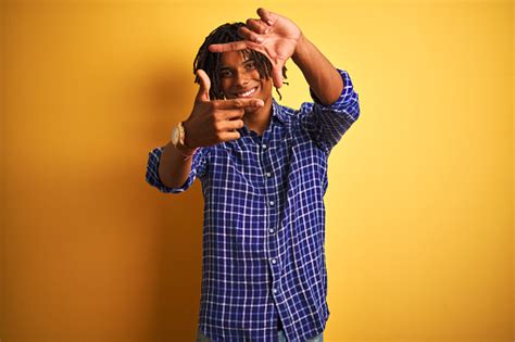 고립 된 노란색 배경 위에 서있는 캐주얼 셔츠를 입고 공포를 가진 아프로 남자는 행복한 얼굴로 손과 손가락으로 프레임을 만드는 미소 창의력과 사진 개념 개념에 대한 스톡