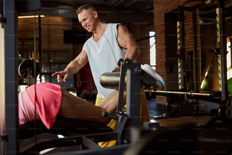 쾌활한 피트니스 코치가 체육관에서 다리 확장 기계에서 여성에게 지시를 내리면서 웃고 있는 자른 사진 사진 Unsplash의 스포츠 이미지