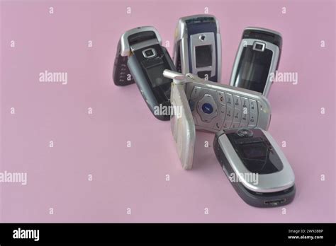 Two Vintage Flip Phones Open And Standing Among Other Models On A Pink Background Old Cellular