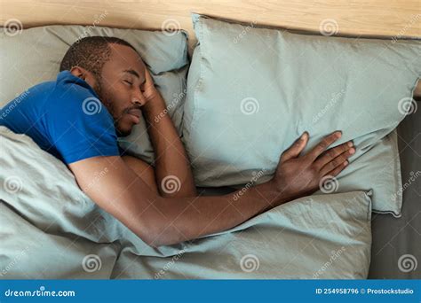 African Man Sleeping Alone Touching Pillow Lying In Bed Indoors Stock