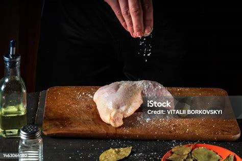요리사는 어두운 배경에 바다 소금으로 신선한 생 닭고기 드럼 스틱을 뿌립니다 근처에 요리할 재료와 향신료가 있습니다 요리사에 대한 스톡 사진 및 기타 이미지 Istock