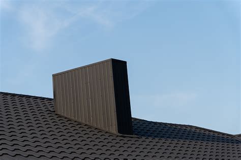 독특한 직사각형 모양의 눈에 띄는 굴뚝이 옥상에서 솟아올라 고요한 푸른 하늘과 대조를 이루며 혁신적인 건축 스타일을 보여줍니다