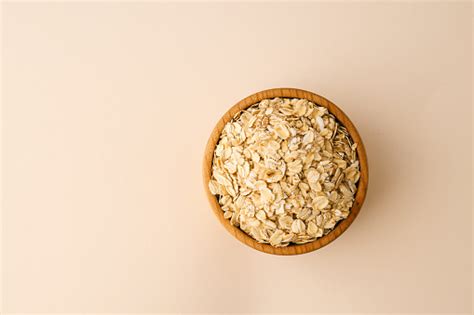 베이지색 배경에 으깬 귀리를 가득 채운 나무 그릇 미니멀한 구성은 귀리의 자연스러운 질감과 색상을 강조하여 단순함과 건강을 강조합니다 건강관리와 의술에 대한 스톡 사진 및