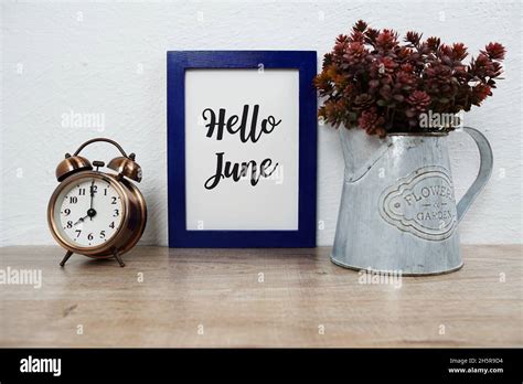 Hello June Typography Text With Alarm Clock And Artificial Plant Decoration On Wooden Table And
