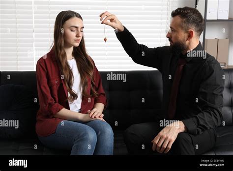 Psychologist using pendulum while working with patient during hypnosis session indoors Stock ...