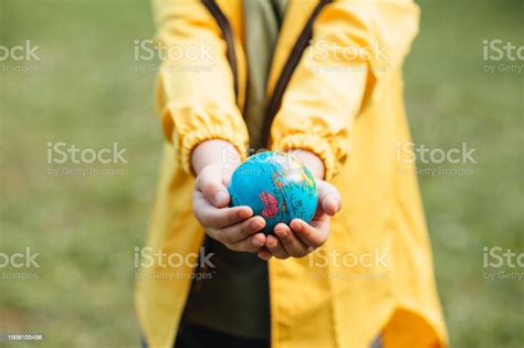 노란 비옷을 입은 어린 소녀가 공원이나 숲에서 야외에서 손에 지구본을 들고 있다 세계 지구의 날 개념입니다 녹색 에너지 재생 가능하고 지속 가능한 자원 지구를 보호하고