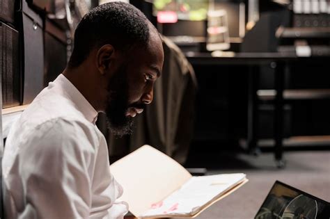 Premium Photo Policeman Reading Crime Case File And Analyzing Photos On Laptop African