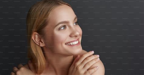 행복을 표현하고 회색 배경에 고립되어 있는 동안 미소로 먼 곳을 바라보는 긍정적인 젊은 여성의 클로즈업 사진 Unsplash의 어깨에 손을 이미지