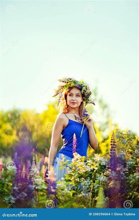 Девушка с венком цветов на голове сидит на закате в поле с фиолетовыми цветами люпина