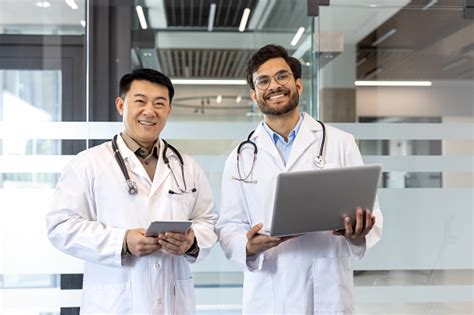 두 명의 의사가 노트북과 태블릿을 갖춘 현대적인 의료 사무실에 자신 있게 서서 디지털 의료 협업과 팀워크를 보여줍니다 전문적인 의료 환경을 대표하는 데 이상적입니다 2명에