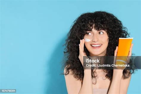 밝은 파란색 배경에 얼굴에 자외선 차단 크림을 바르고 있는 자외선 차단제 튜브를 가진 아름다운 젊은 여성 텍스트를 위한 공간 20 24세에 대한 스톡 사진 및 기타 이미지