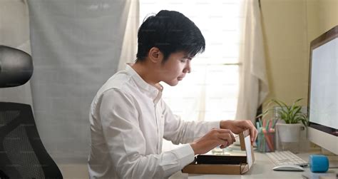 똑똑한 남자가 흰색 작업 책상에서 온라인 쇼핑에서 골판지 상자를 개봉하고 있습니다 사진 Unsplash의 태국 이미지