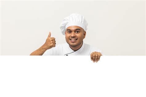 해피 영 잘 생긴 제복을 입은 아시아 남자 셰프가 빈 화이트보드 뒤에서 밖을 내다본다 부엌과 식당에서 텍스트 메뉴를 광고하기 위해 큰 빈 광고판 뒤에 숨어있는 인도 남자