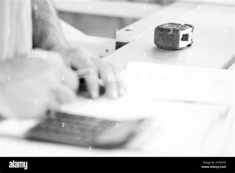Carpenter Calculating Costs In His Workshop Using A Calculator With Tape Measure And Pencil