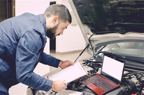 균일 한 잘생긴 젊은 자동차 정비사는 자동 서비스에서 자동차를 검사 하는 동안 메모를 만드는 것입니다 가까운에 대한 스톡 사진
