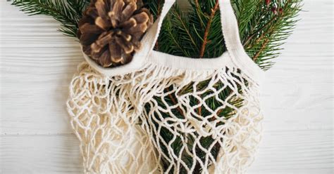 흰색 소박한 배경에 녹색 가문비나무 가지와 솔방울이 있는 재사용 가능한 면 가방 겨울 장식 제로 폐기물 휴일과 그물 쇼핑백