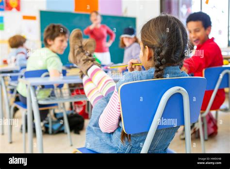 Rear View Of Primary Schoolgirl With Feet On Desk In Classroom Stock