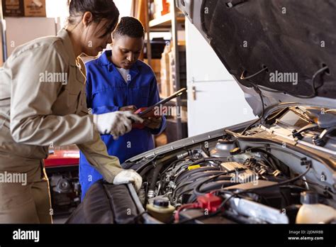 Mid Adult Multiracial Female Mechanics Using Digital Tablet While Repairing Car S Engine Stock